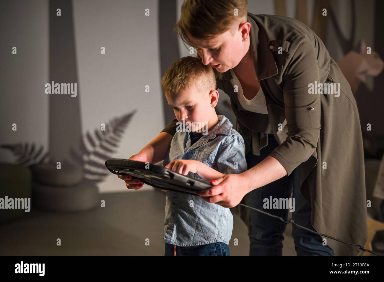 Child boy using touch screen tablet display in a museum with his mother ...
