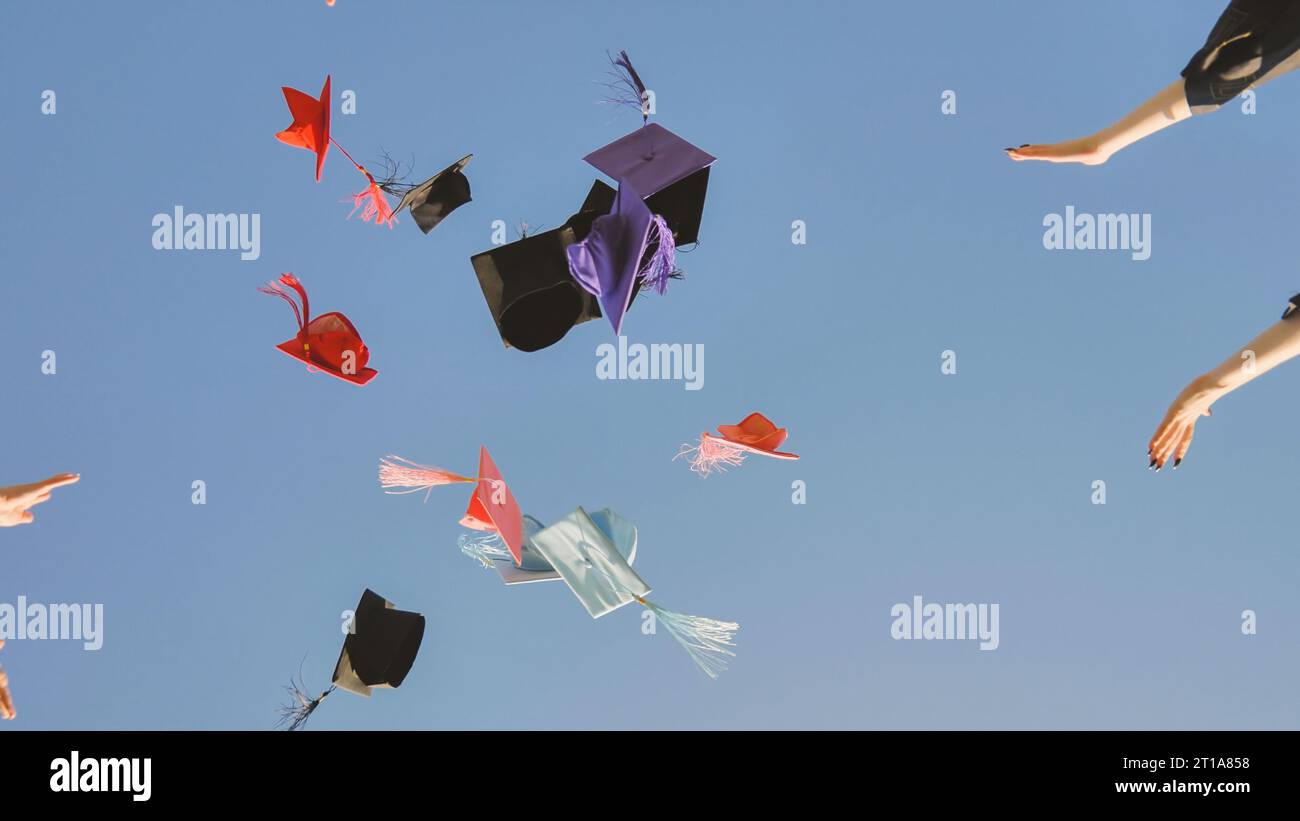 Happy college graduates standing in a circle tossing colorful hats up ...