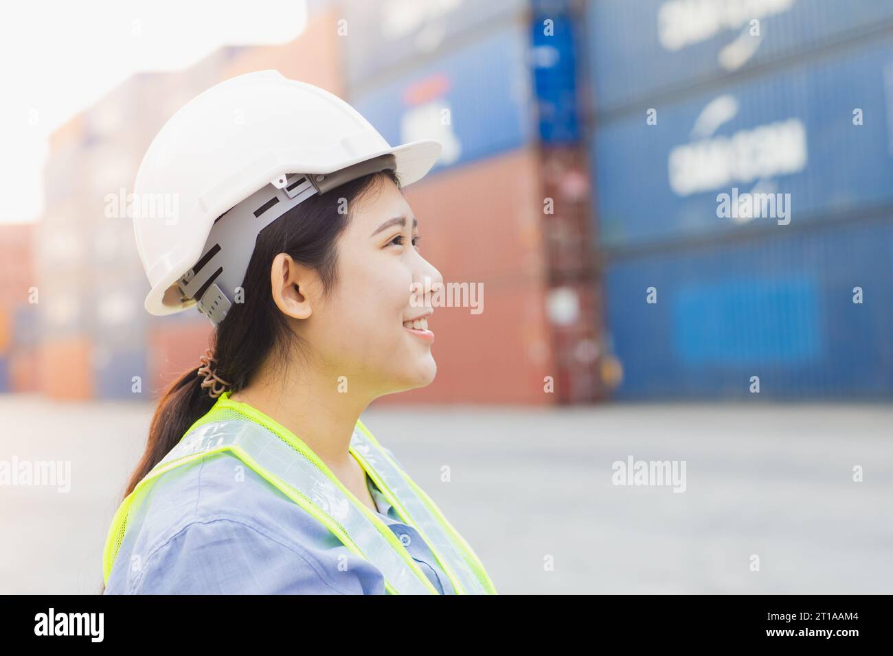 Asian woman happy dock worker control loading containers cargo at shipyard. Marine and carrier ...