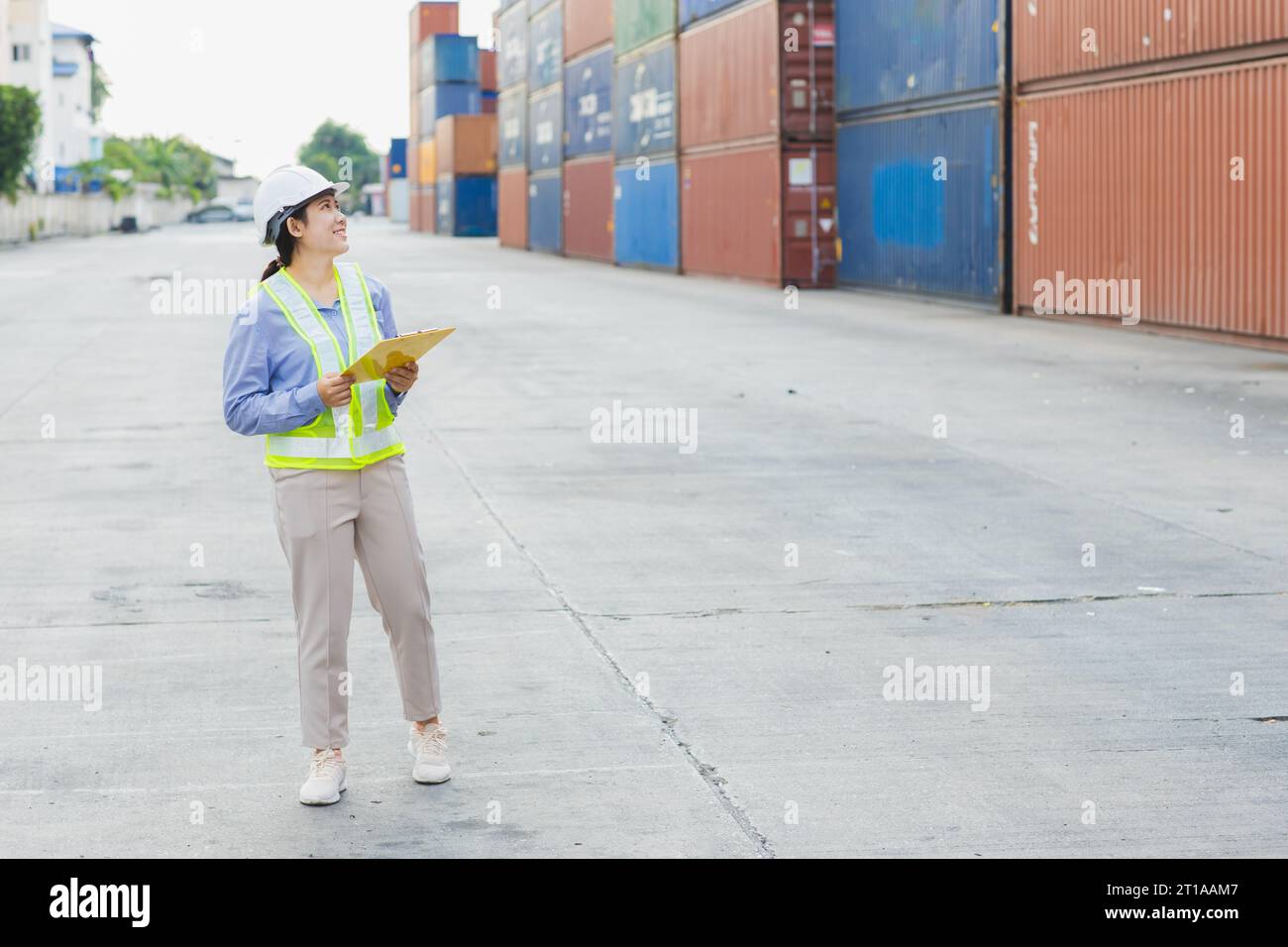 Asian woman happy dock worker control loading containers cargo at shipyard. Marine and carrier ...