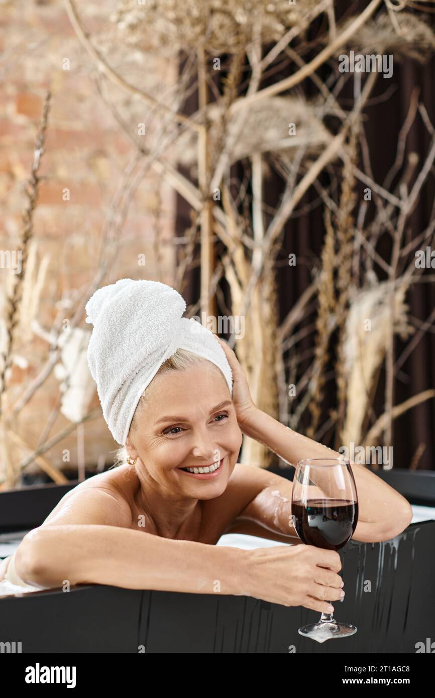 dreamy middle aged woman with towel on head holding glass of red wine while taking bath Stock ...