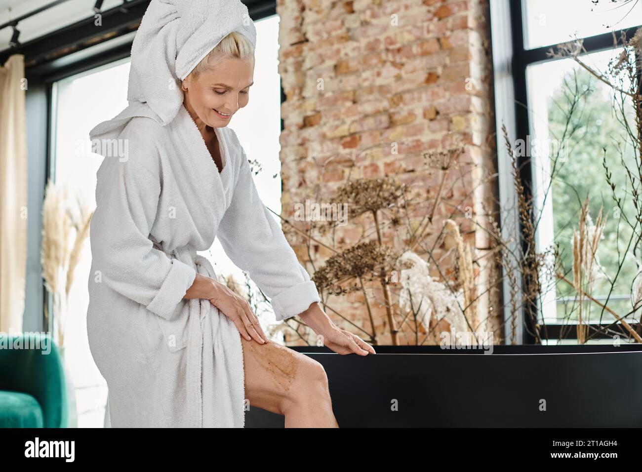 happy middle aged woman in bathrobe and with towel on head applying ...