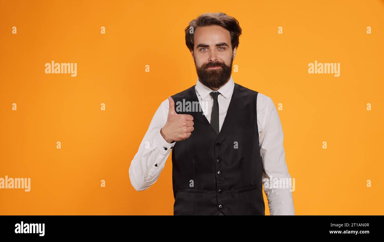 Stylish butler shows thumbs up gesture in studio, indicating positive ...