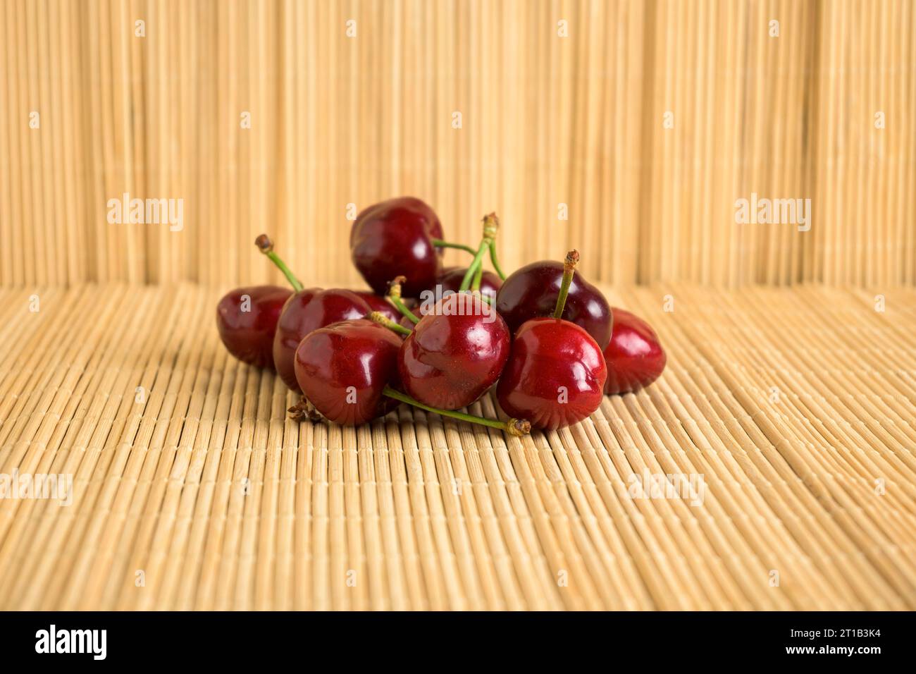 ripe red cherries with green stem ready to eat on light bamboo ...
