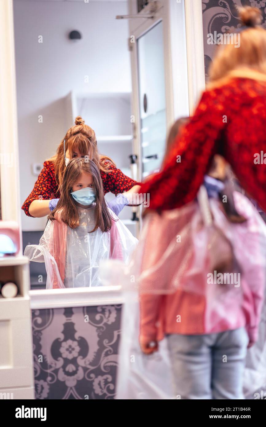 Hairdresser with mask and gloves cutting a girl's hair with scissors ...