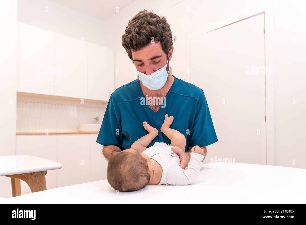 Portrait of a young doctor checking up a baby lying down on stretcher ...