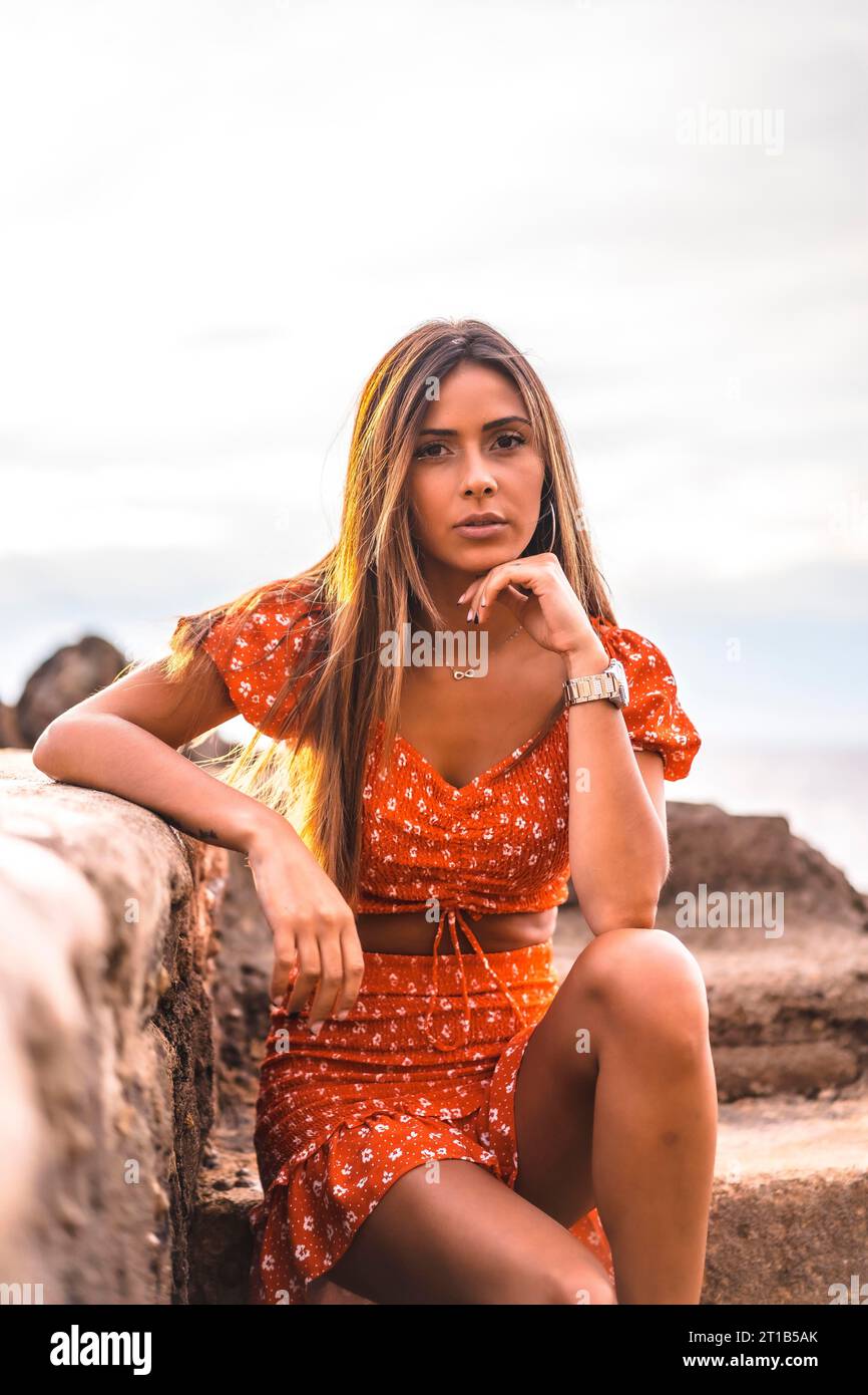 A young brunette Caucasian woman in a red dress on the beach of ...