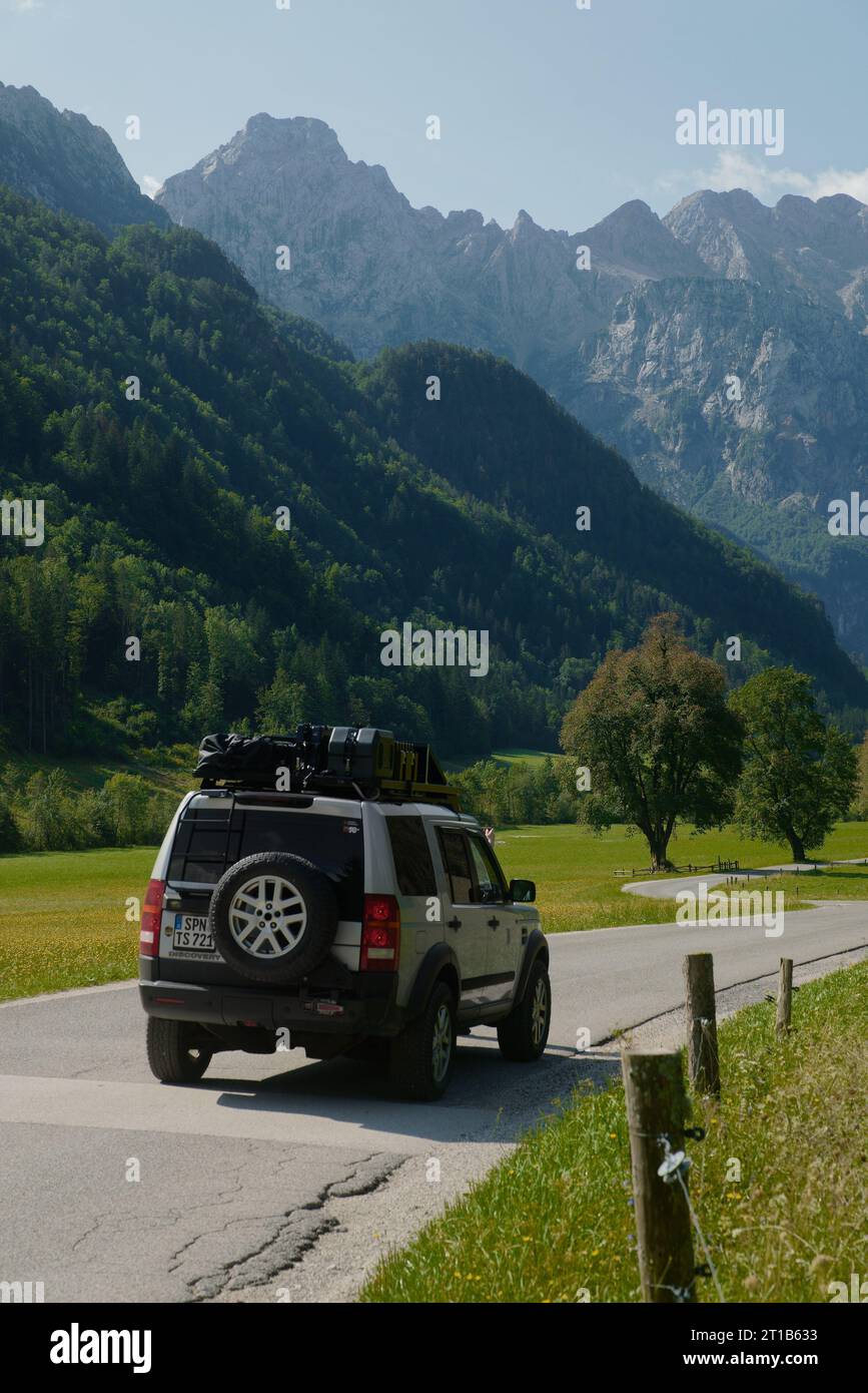A white SUV driving down a rural road surrounded by mountains and a ...