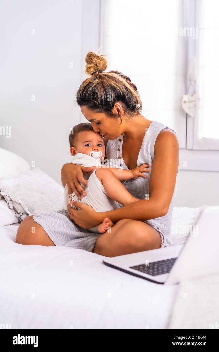 Young Caucasian mother with her son in the room on top of the bed. Baby less than a year ...