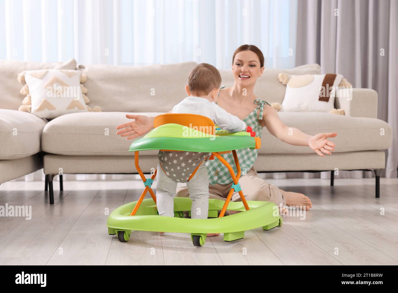 Little boy in baby walker hurrying to happy mother at home. Woman ...