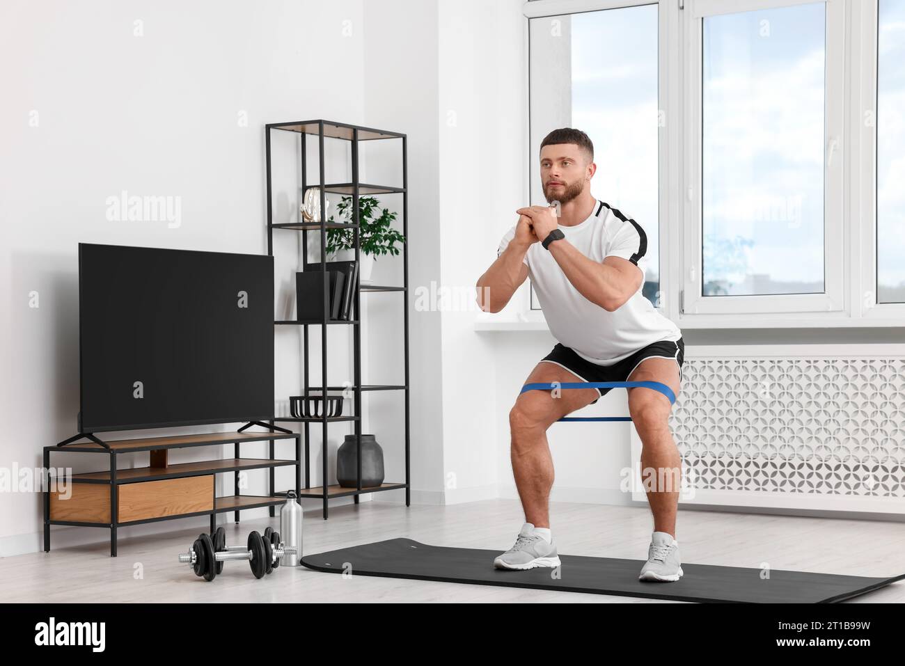 Athletic man doing exercise with elastic resistance band on mat at home ...