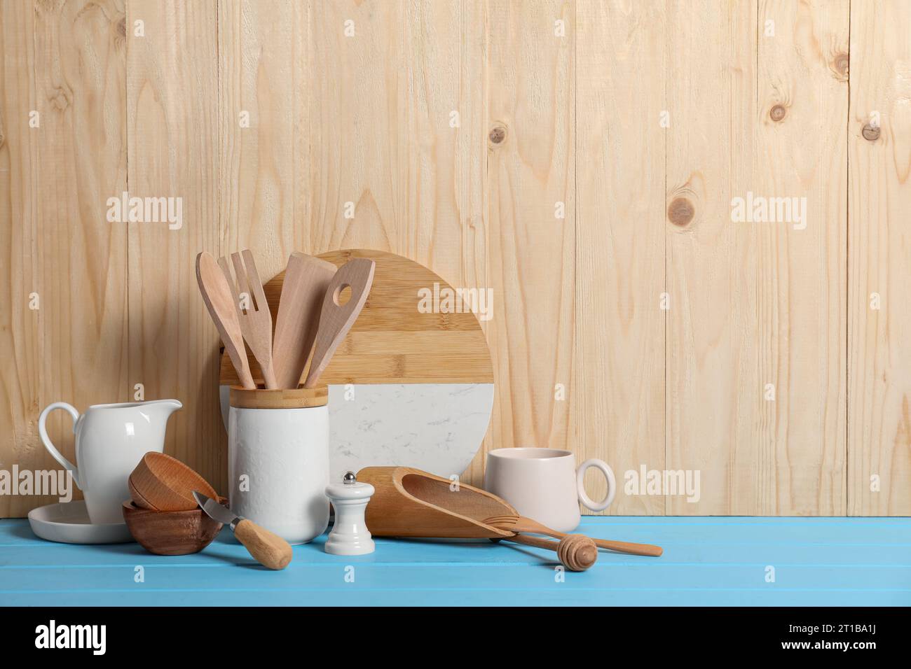 Set of different kitchen utensils on light blue table against wooden ...