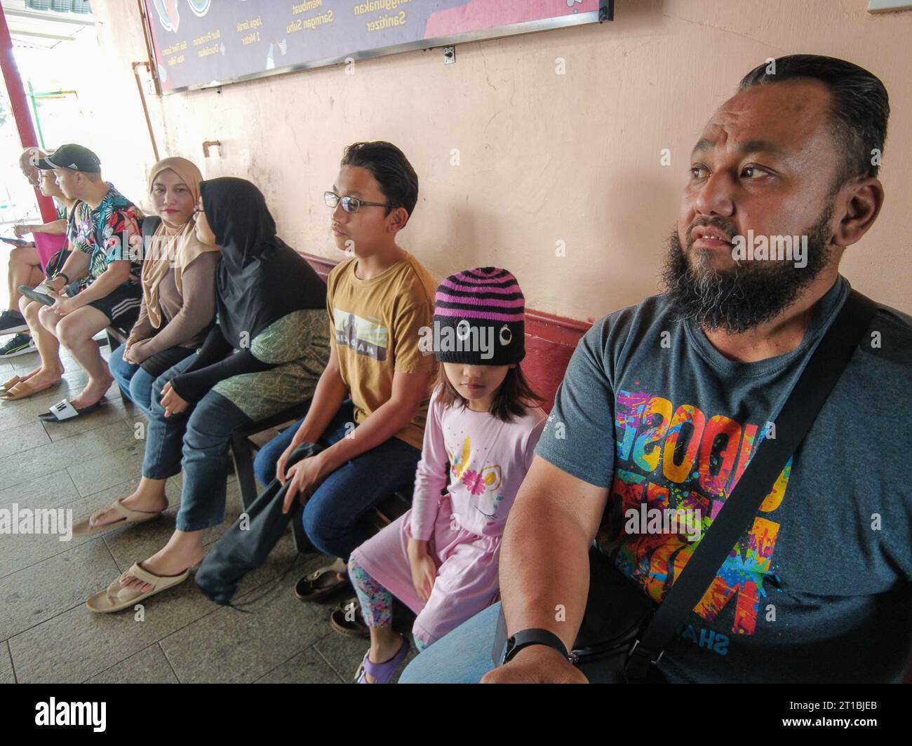 Melaka, Malaysia - July 9, 2023 Asian Malay family waiting and sitting at the bus stop, waiting ...