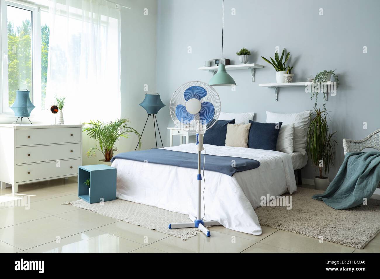 Interior of light bedroom with cozy bed and floor fan Stock Photo - Alamy