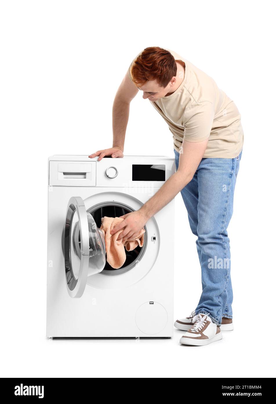 Young man putting laundry into washing machine on white background ...