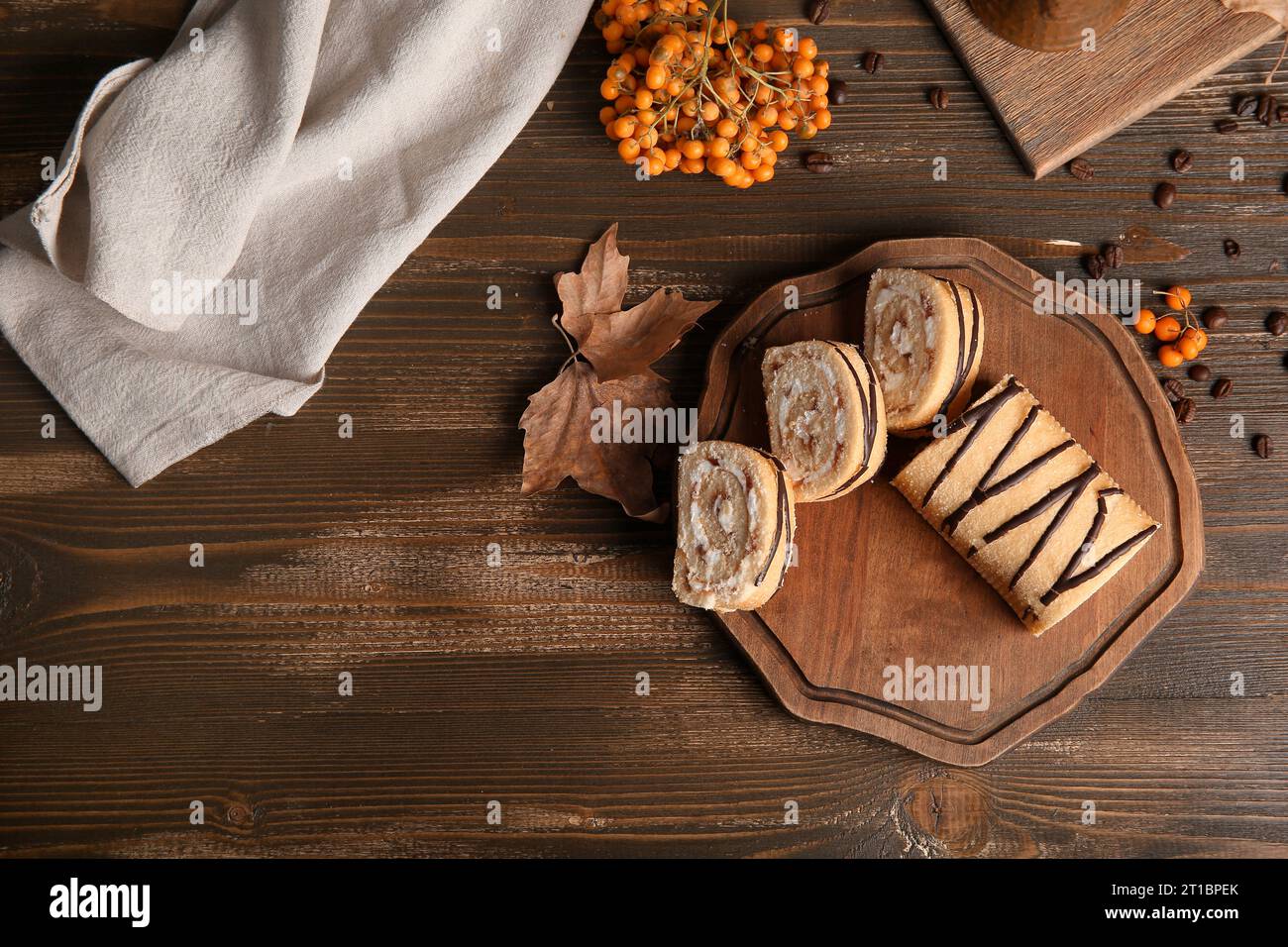 Board with sweet cut sponge cake roll and rowan on wooden background ...