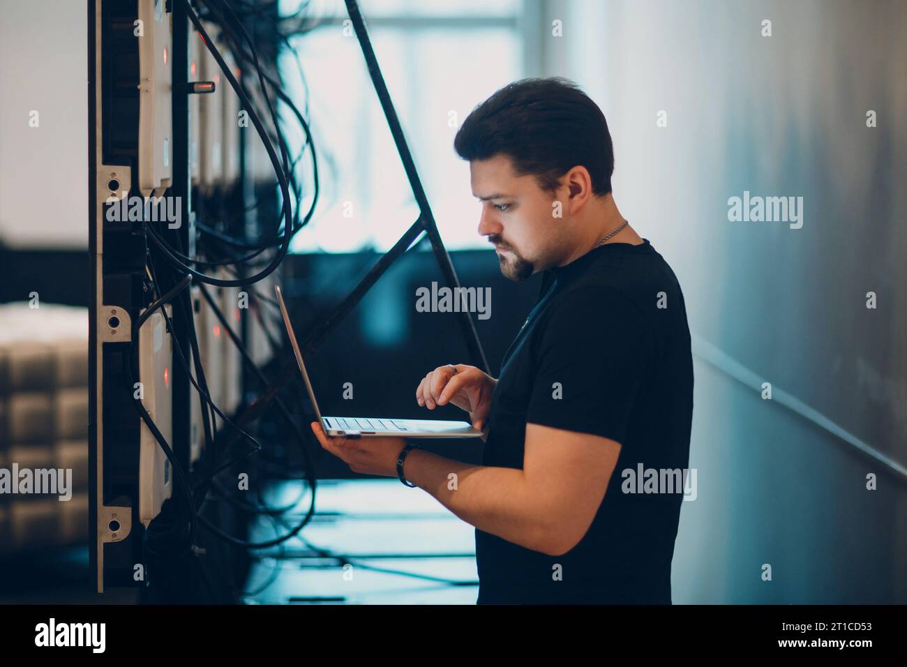 System administrator working on laptop standing near multi-screen LED ...