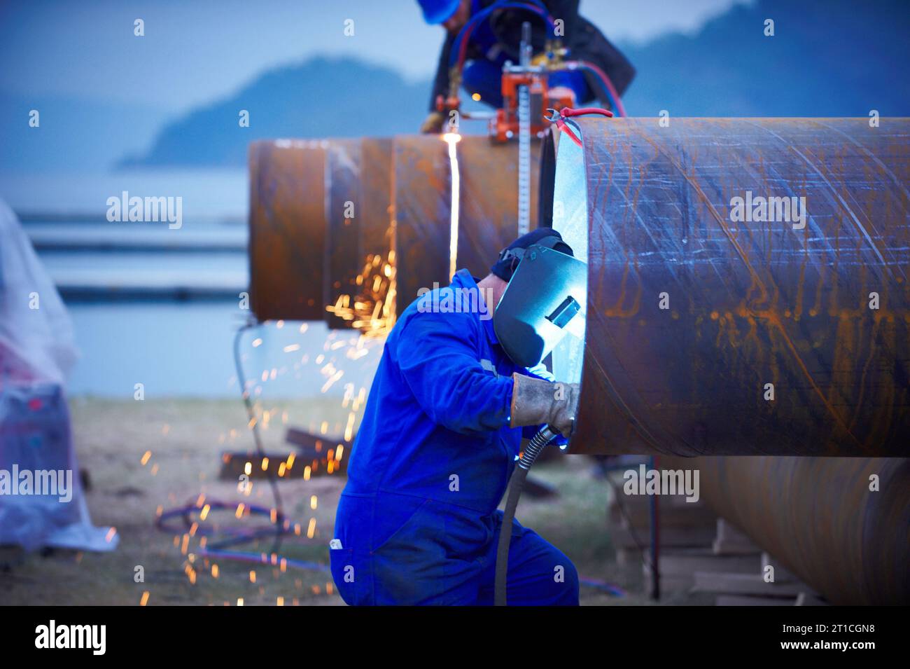 Industrial electrode welder with face shield and blue overall welding a ...