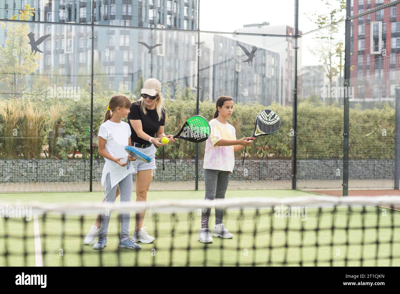 Cheerful coach teaching child to play tennis while both standing on ...