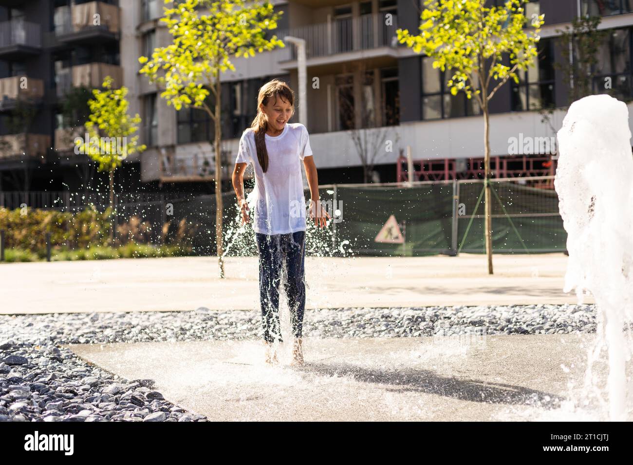 Cheerful young teen girl in city fountain, girl in wet clothes is ...