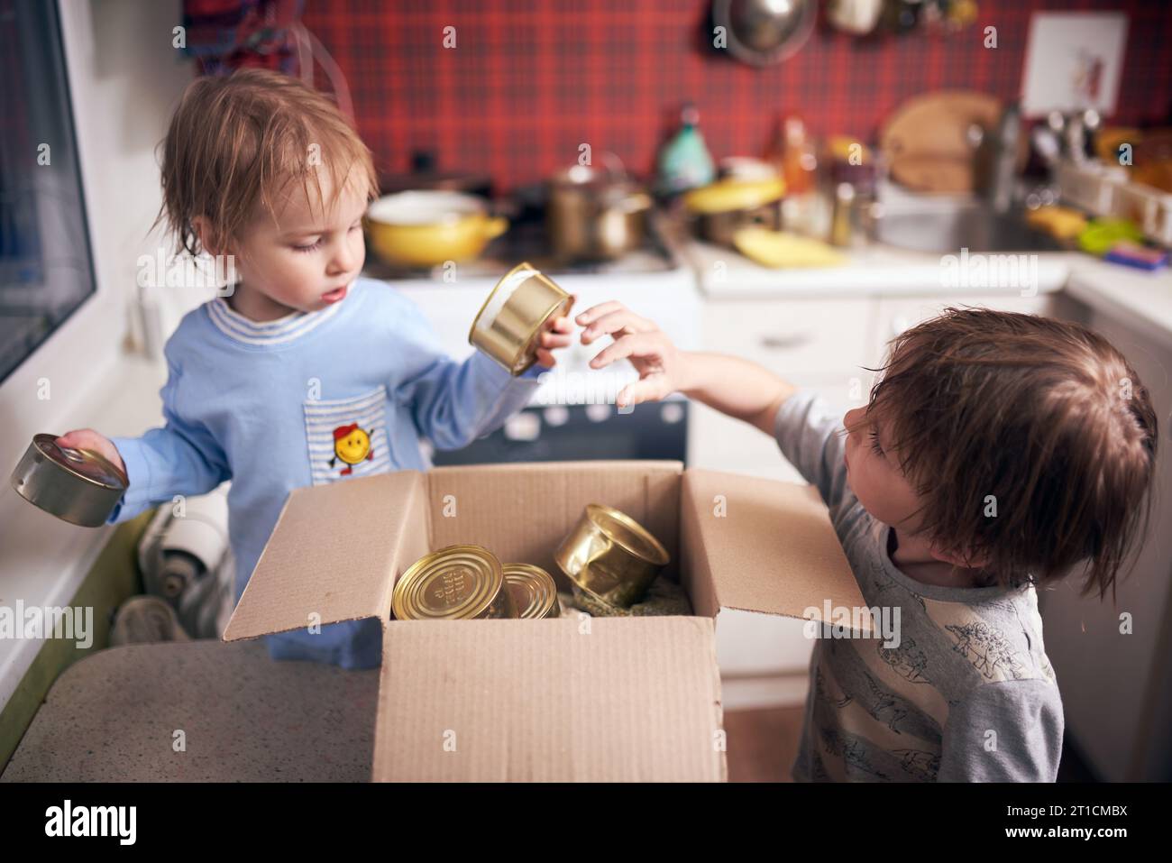 A cute children pulls metal cans out of a box in the kitchen at home ...