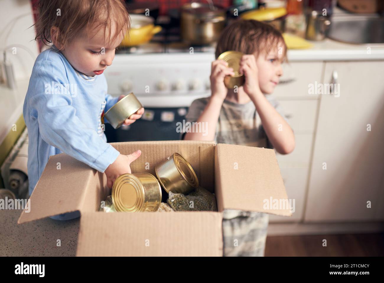 A cute children pulls metal cans out of a box in the kitchen at home ...