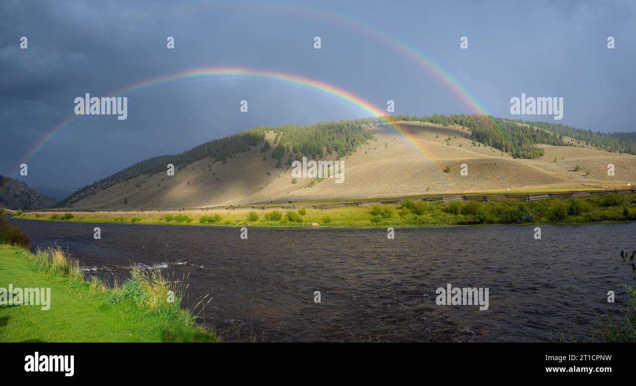 Vibrant double rainbow arches over majestic river and mountain ...