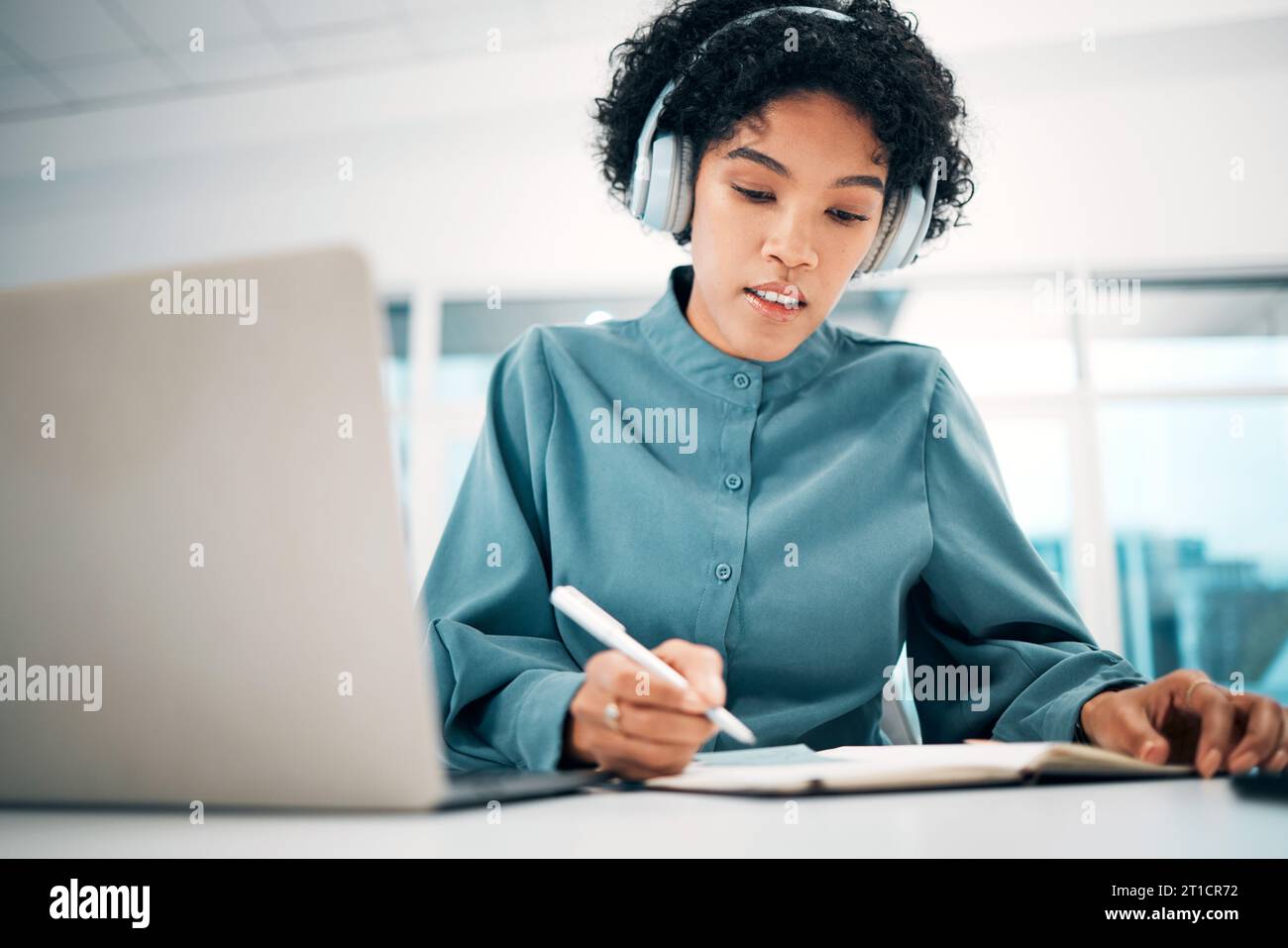 Headphones, laptop and woman writing notes in the office doing research ...