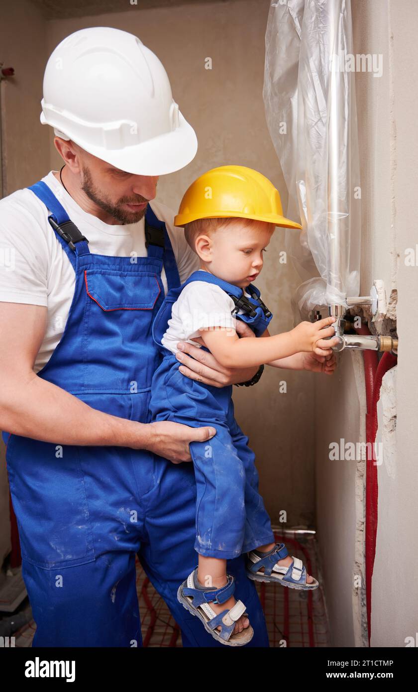 Male plumber holding little boy while child installing plumbing pipes ...