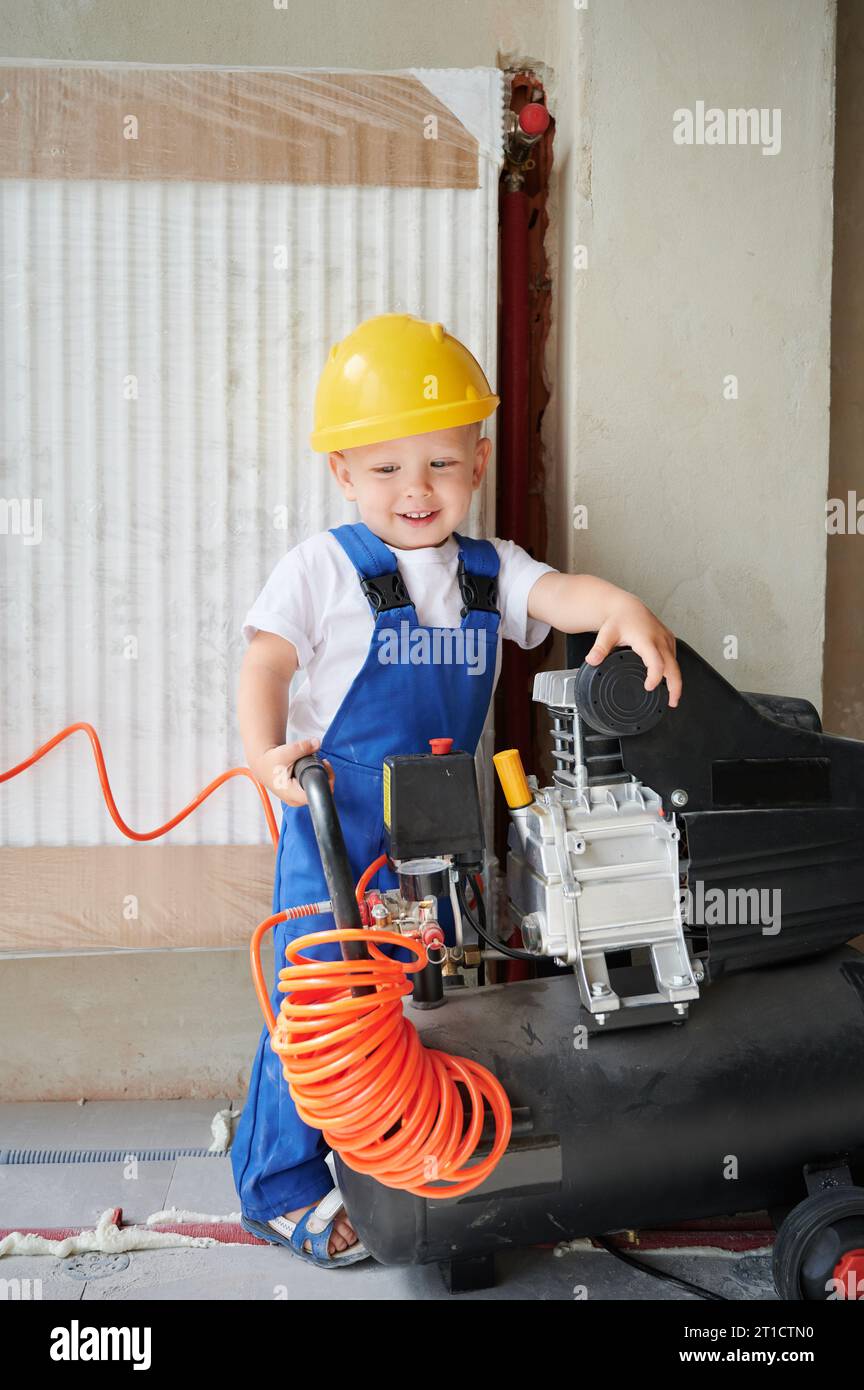 Adorable baby boy in work overalls using industrial high pressure air ...