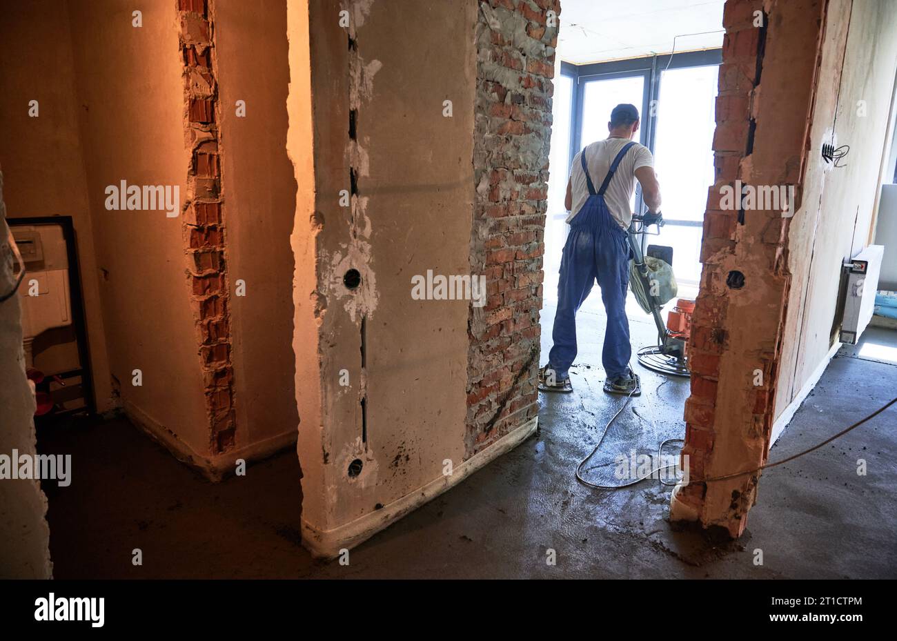 Worker using troweling machine while screeding floor in apartment under ...