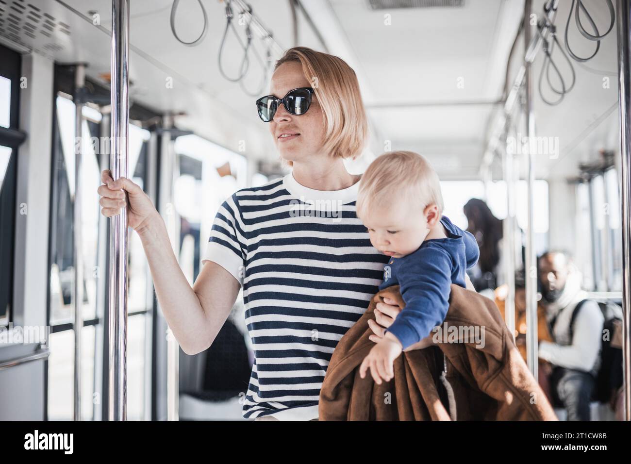 Mother carries her child while standing and holding on to bar holder on ...