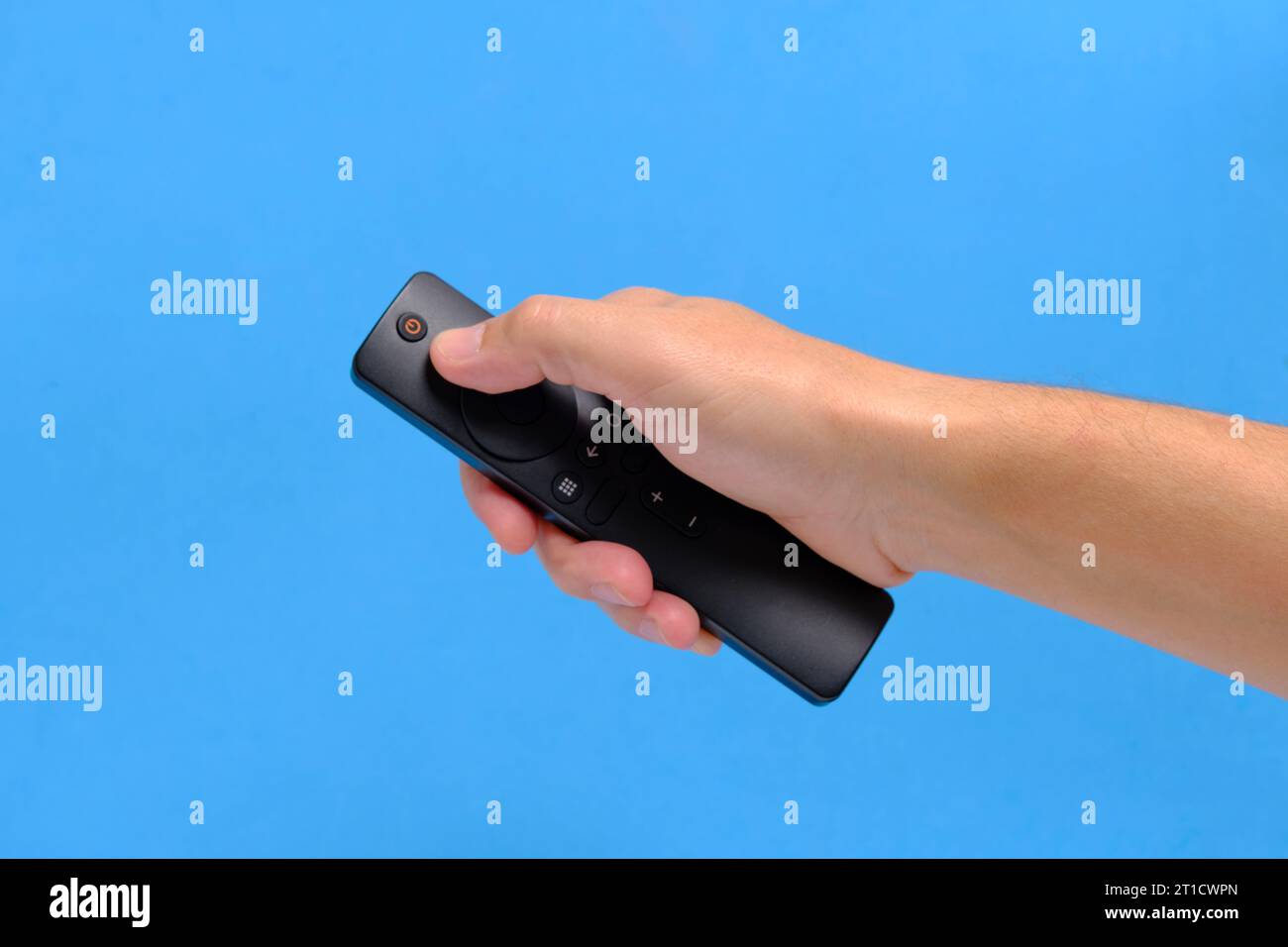 Hand blue background holds TV remote by pressing button with finger ...