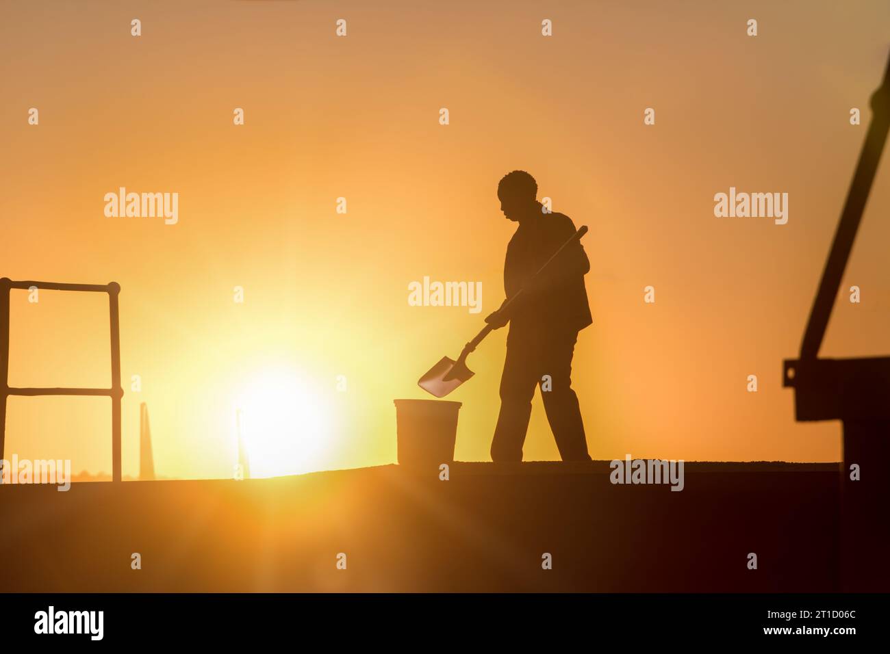 silhouette of an african man with a shovel and bucket loading at sunset ...