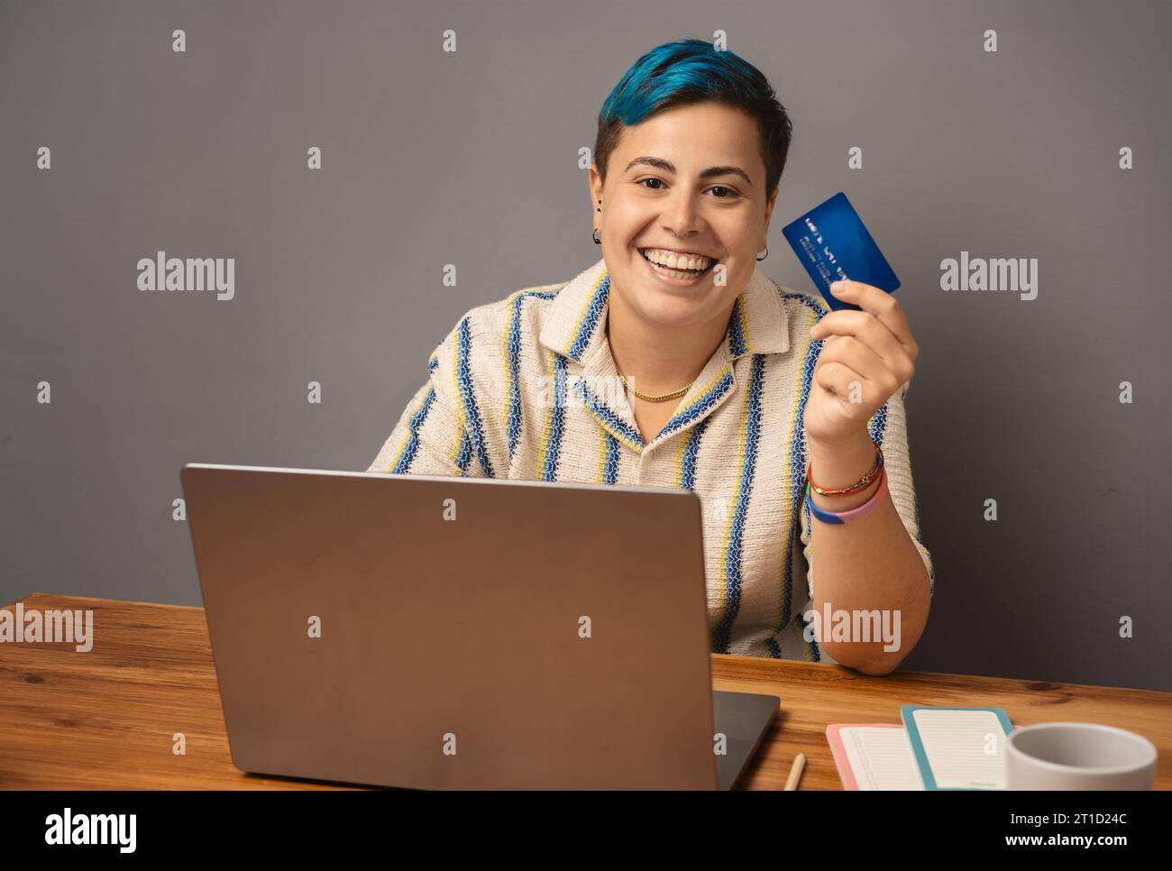 A cheerful individual with vibrant blue hair showcases a credit card ...