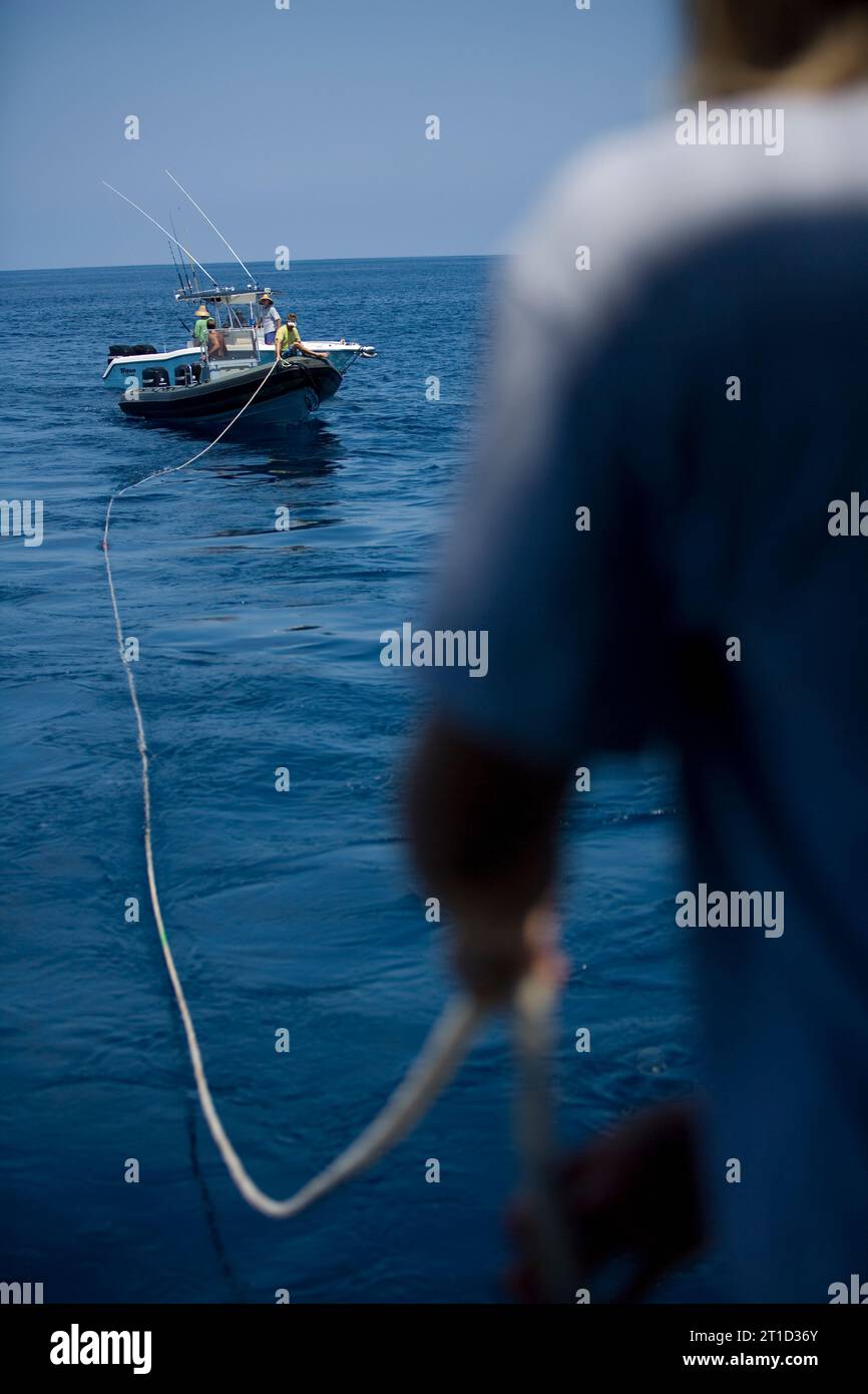 A man pulls on a rope attached to a distant boat, floating toward him ...