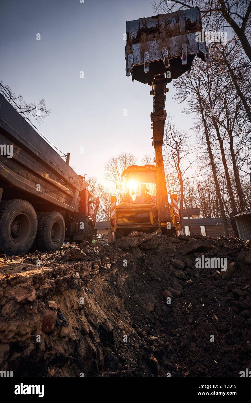 Excavator digs a hole in the ground to build a house at sunset, no ...