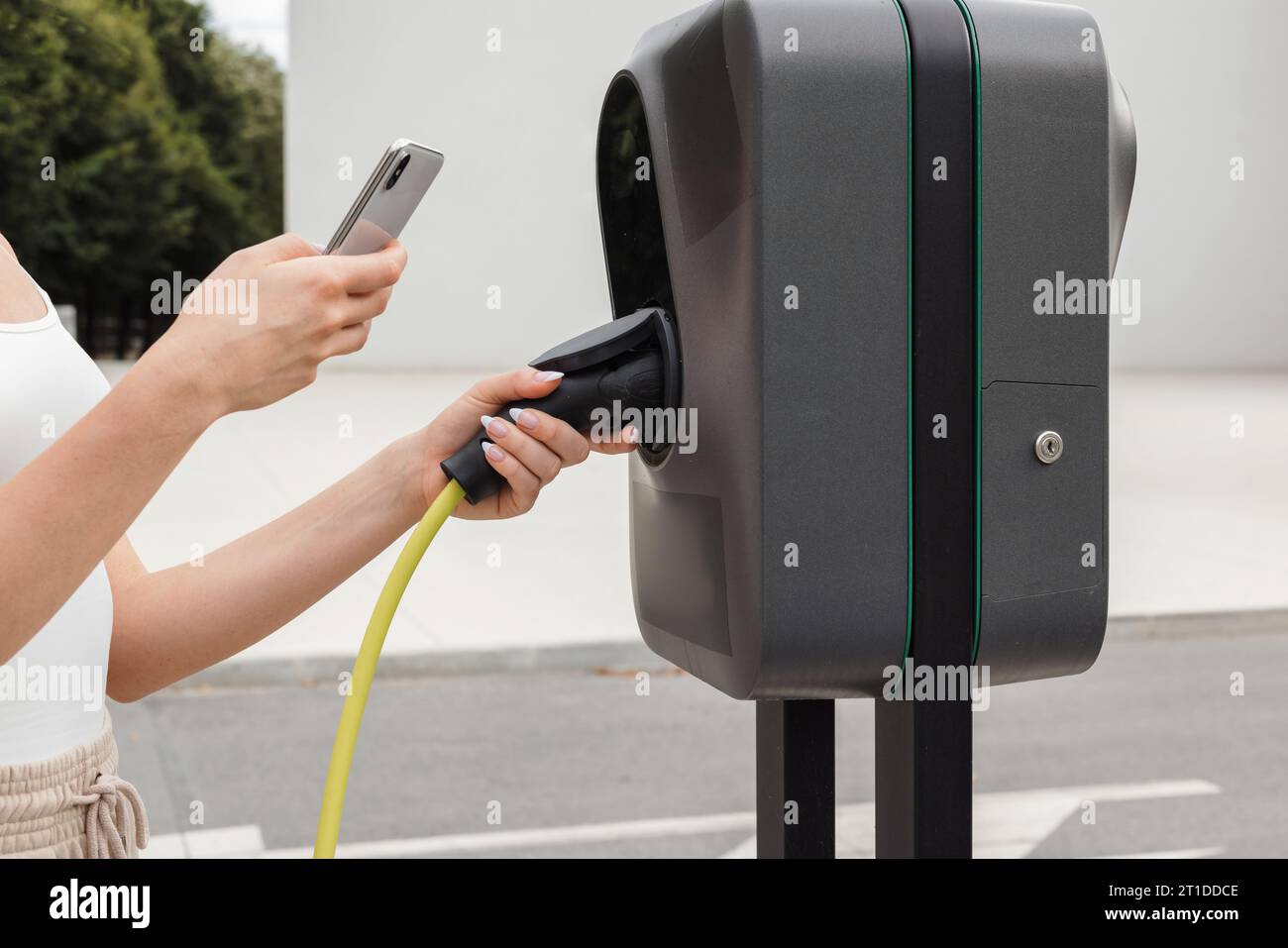 Girl connecting her electric car and a charging station with a cable charger and pressing a ...