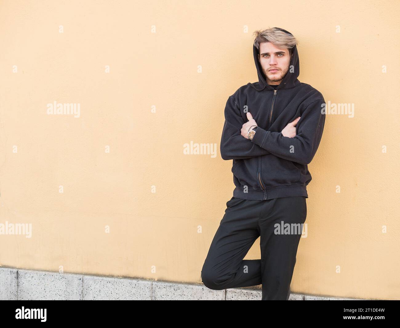 A man leaning against a wall with his arms crossed. Photo of a man with ...