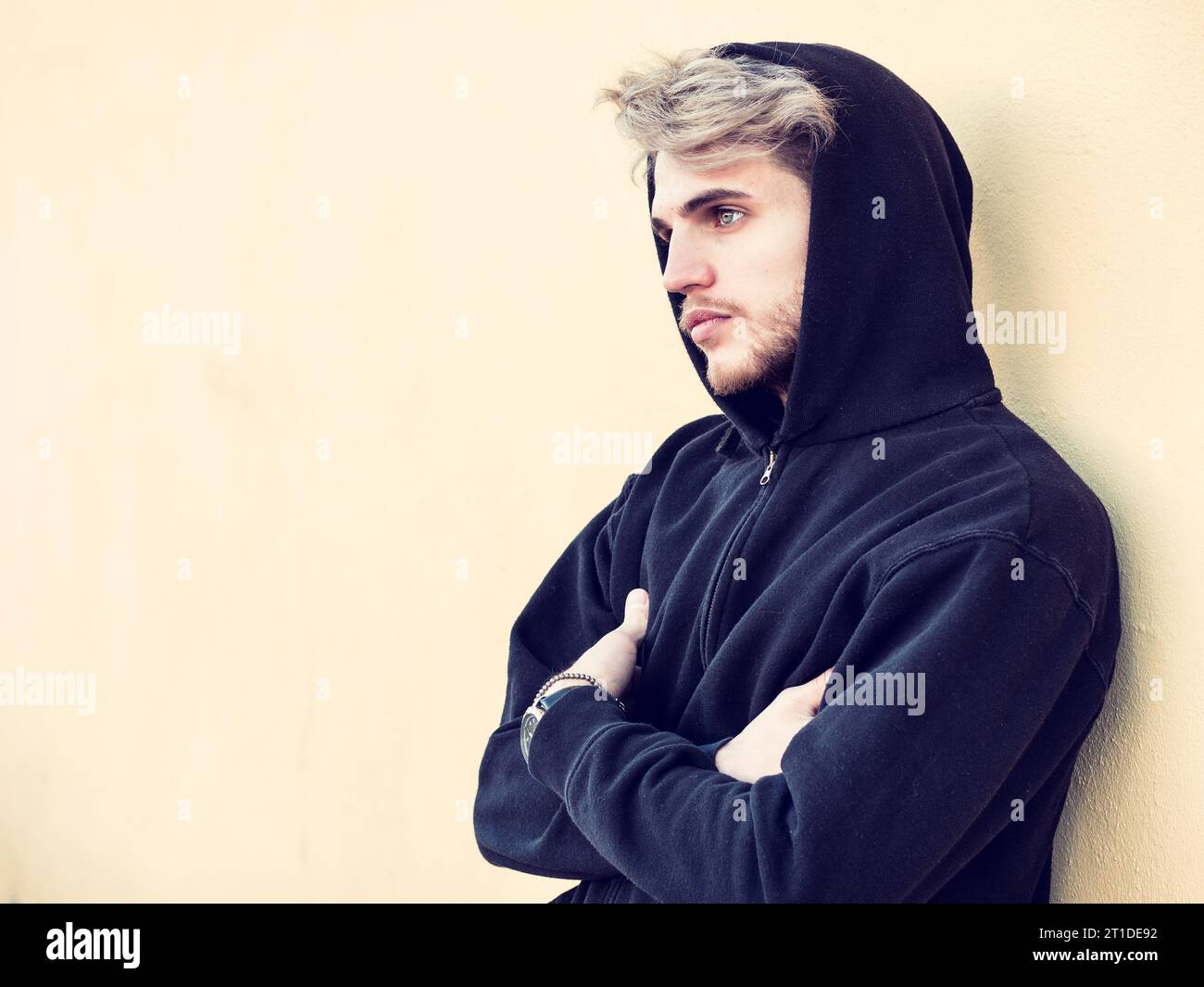A man leaning against a wall with his arms crossed. Photo of a man with ...