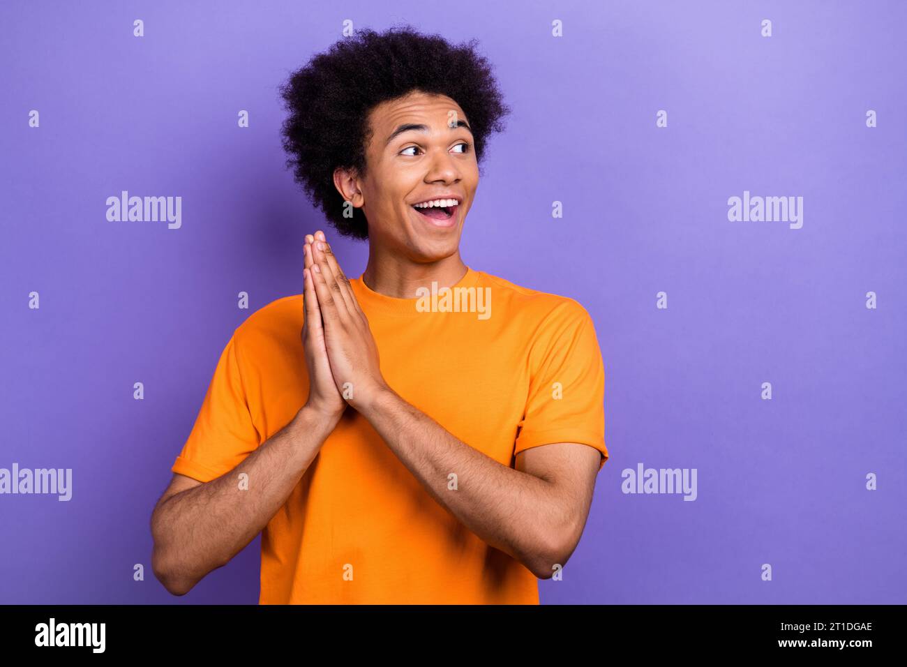 Photo of funky young guy wear orange t shirt palms together dreaming ...