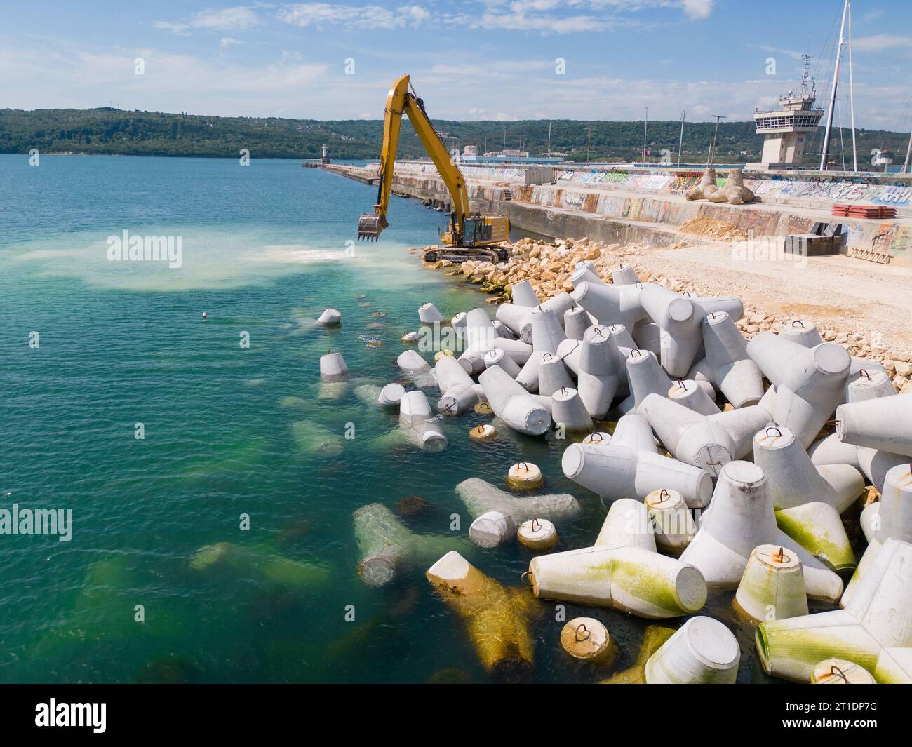 An excavator diligently constructs a dock or breakwater in the sea, its ...