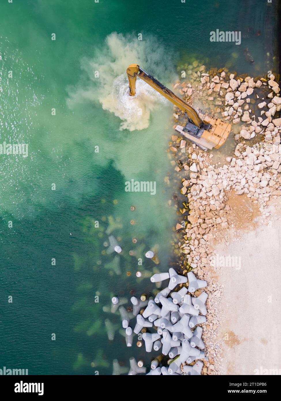 An excavator diligently constructs a dock or breakwater in the sea, its ...
