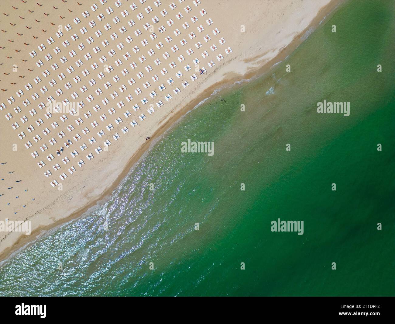 A sandy beach stretches along the seaside, adorned with empty sun ...