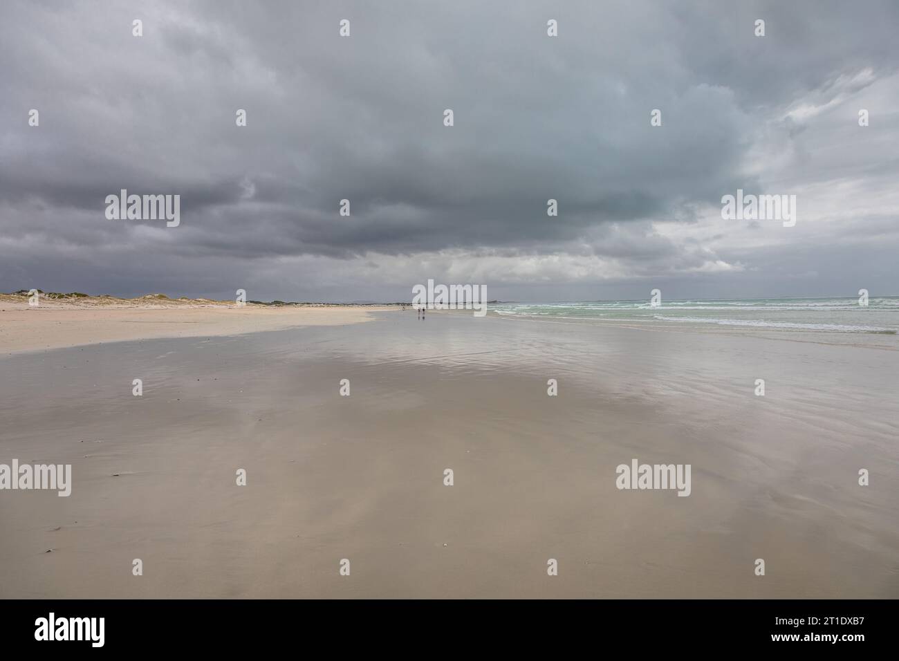 A vast beach is blanketed by grey, stormy clouds, and their reflection glistens on the water as ...