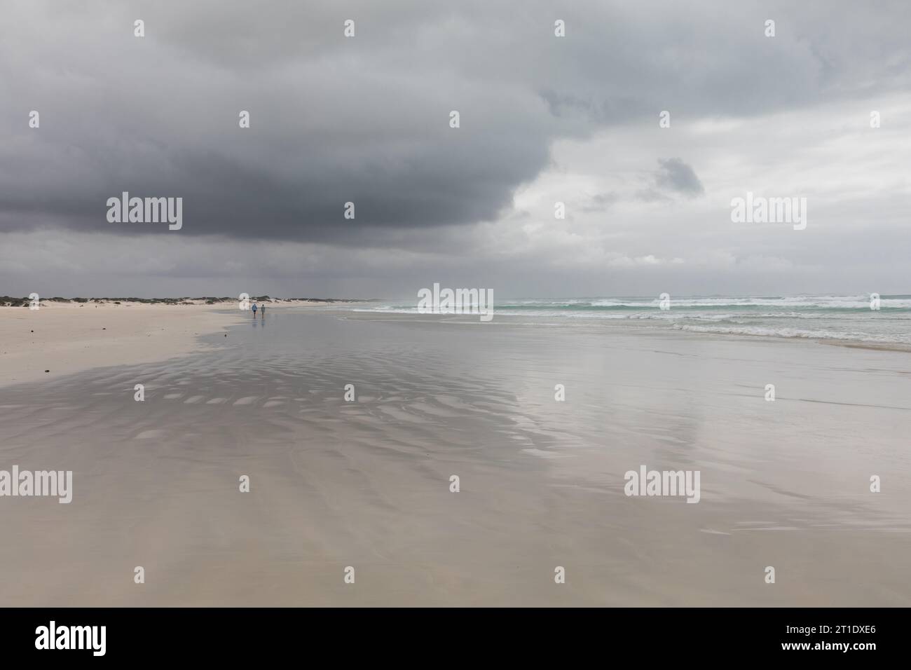 A vast beach is blanketed by grey, stormy clouds, and their reflection ...