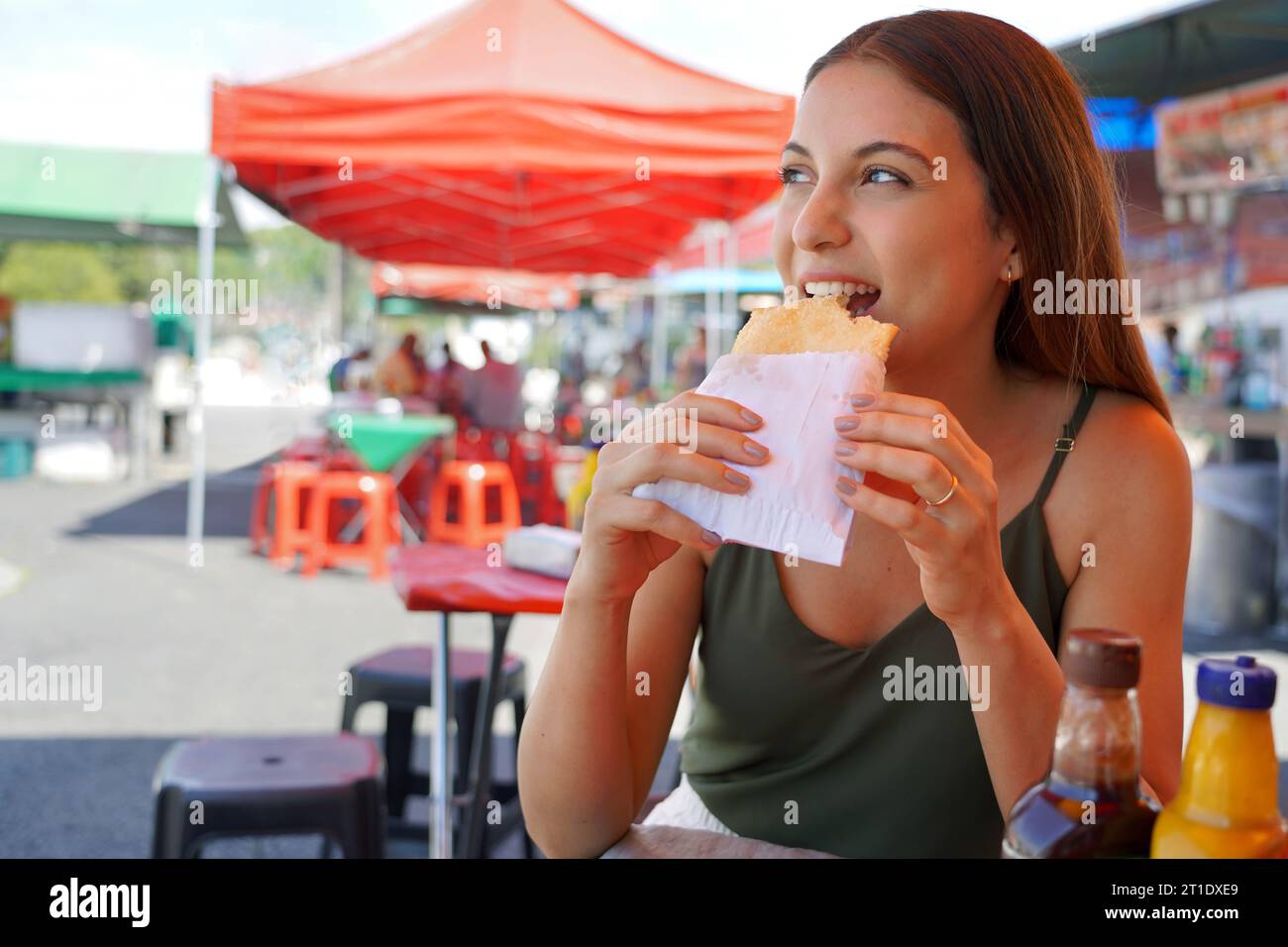 Beautiful young woman eating Brazilian traditional food Pastel de Feira ...