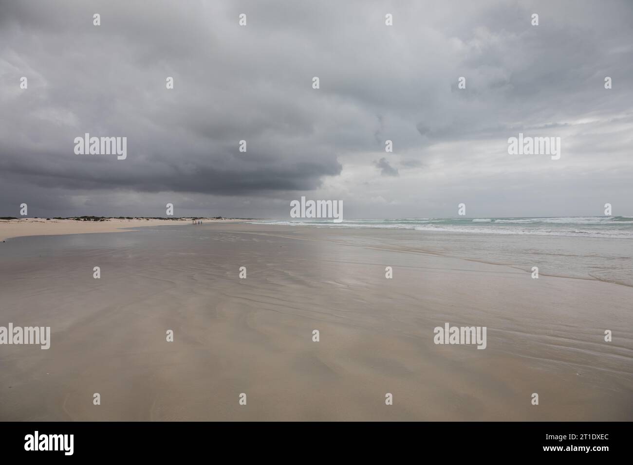 A vast beach is blanketed by grey, stormy clouds, and their reflection ...