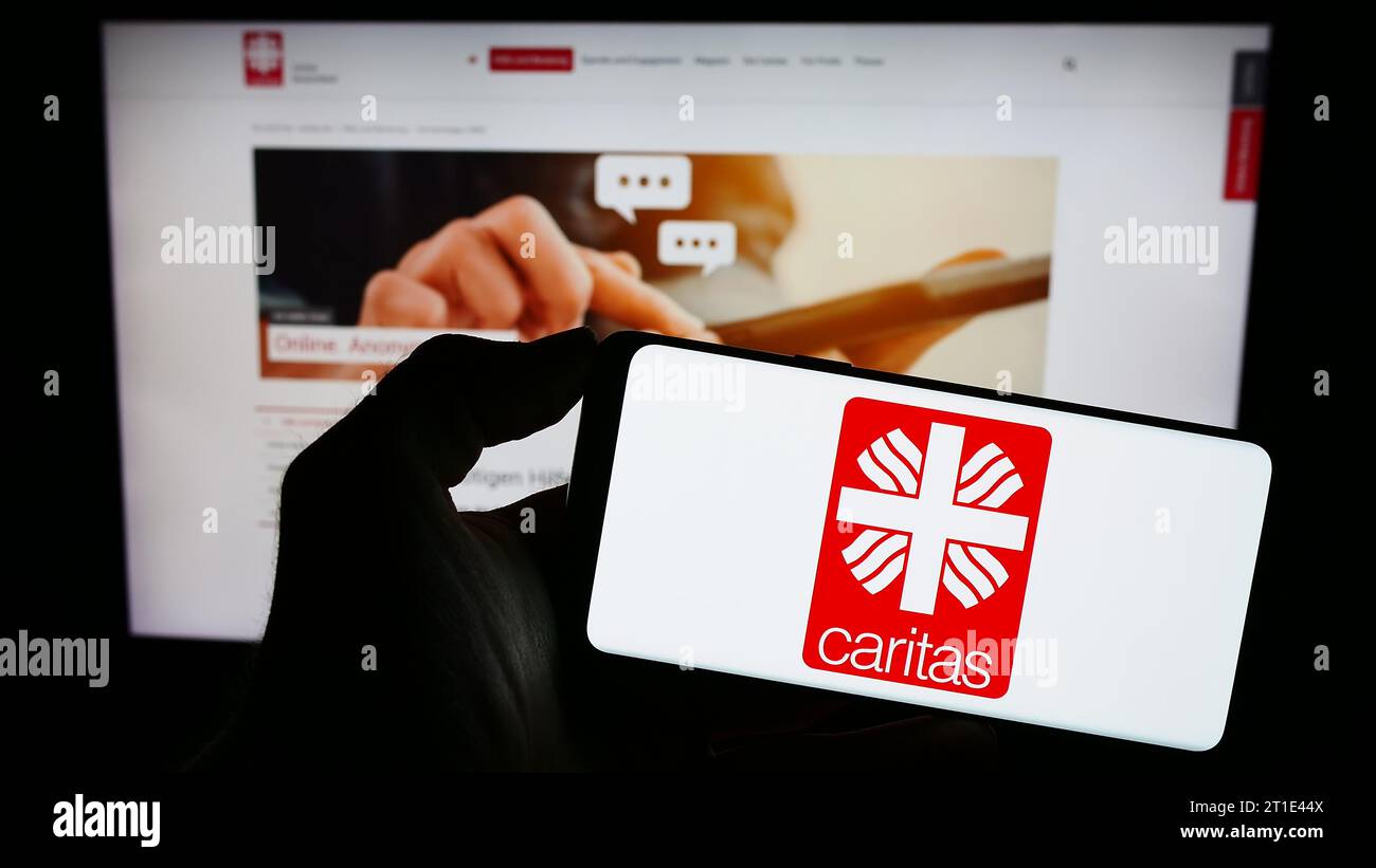 Person holding cellphone with logo of German organization Deutscher Caritasverband e.V. in front ...