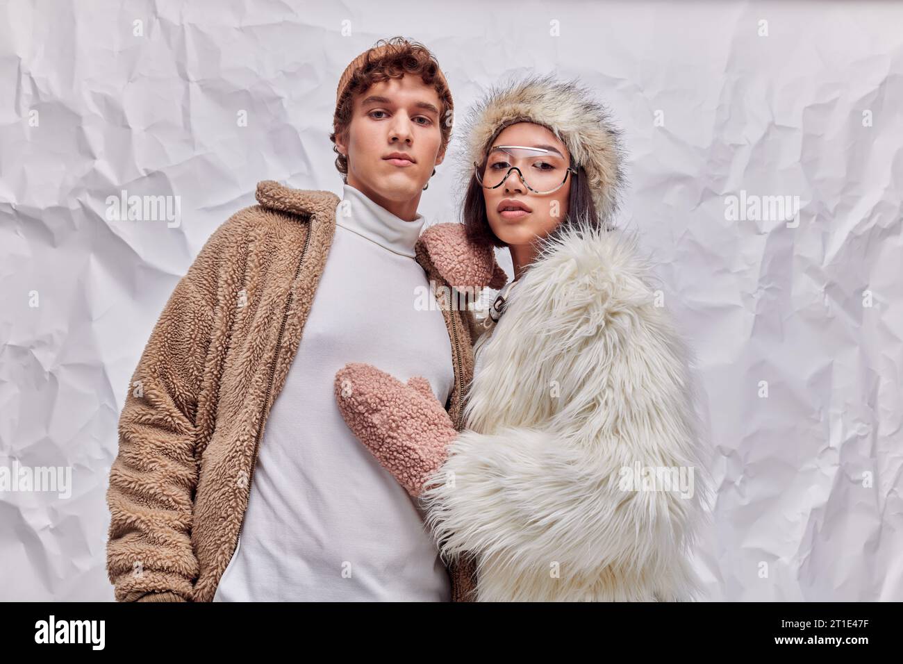 stylish man and asian woman in faux fur jacket and mittens looking at ...